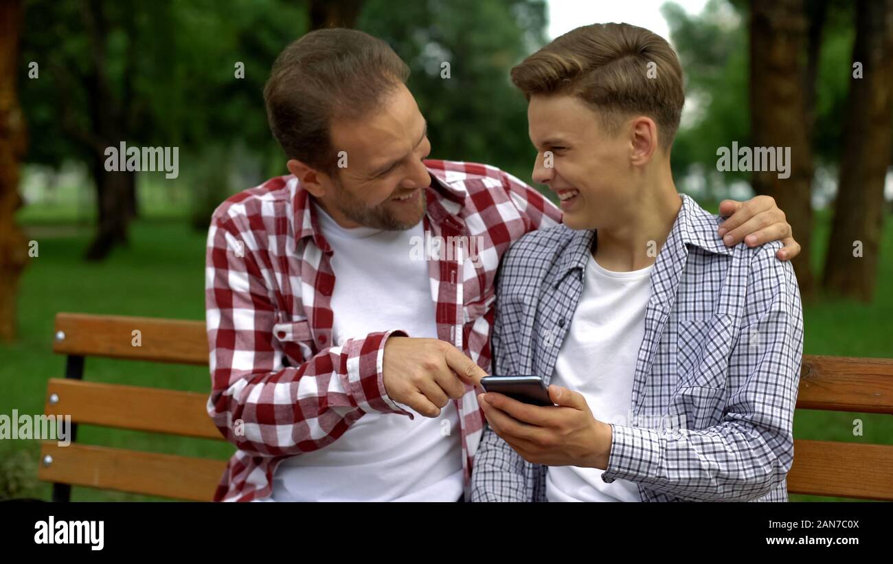 Smiling father and son laughing at funny photo of relative on ...