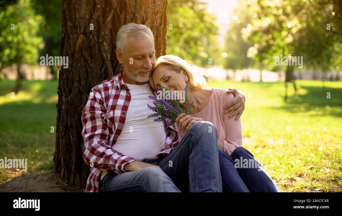 Romantic date of two retired people, man hugging wife with flower ...