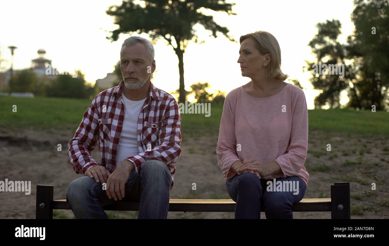 Sorrowful senior couple sitting on bench, wife looking at depressed ...
