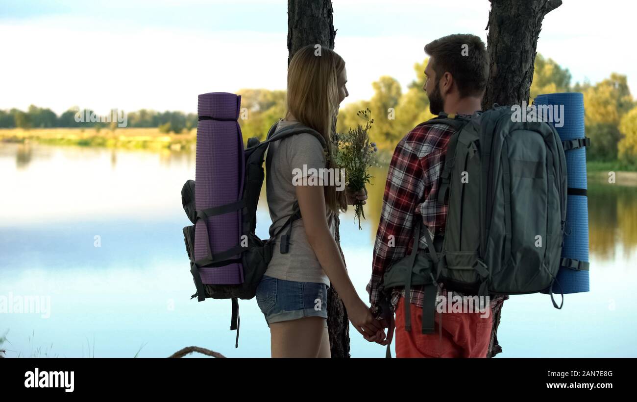Boyfriend with lady watching river scape, holding field flowers, green ...