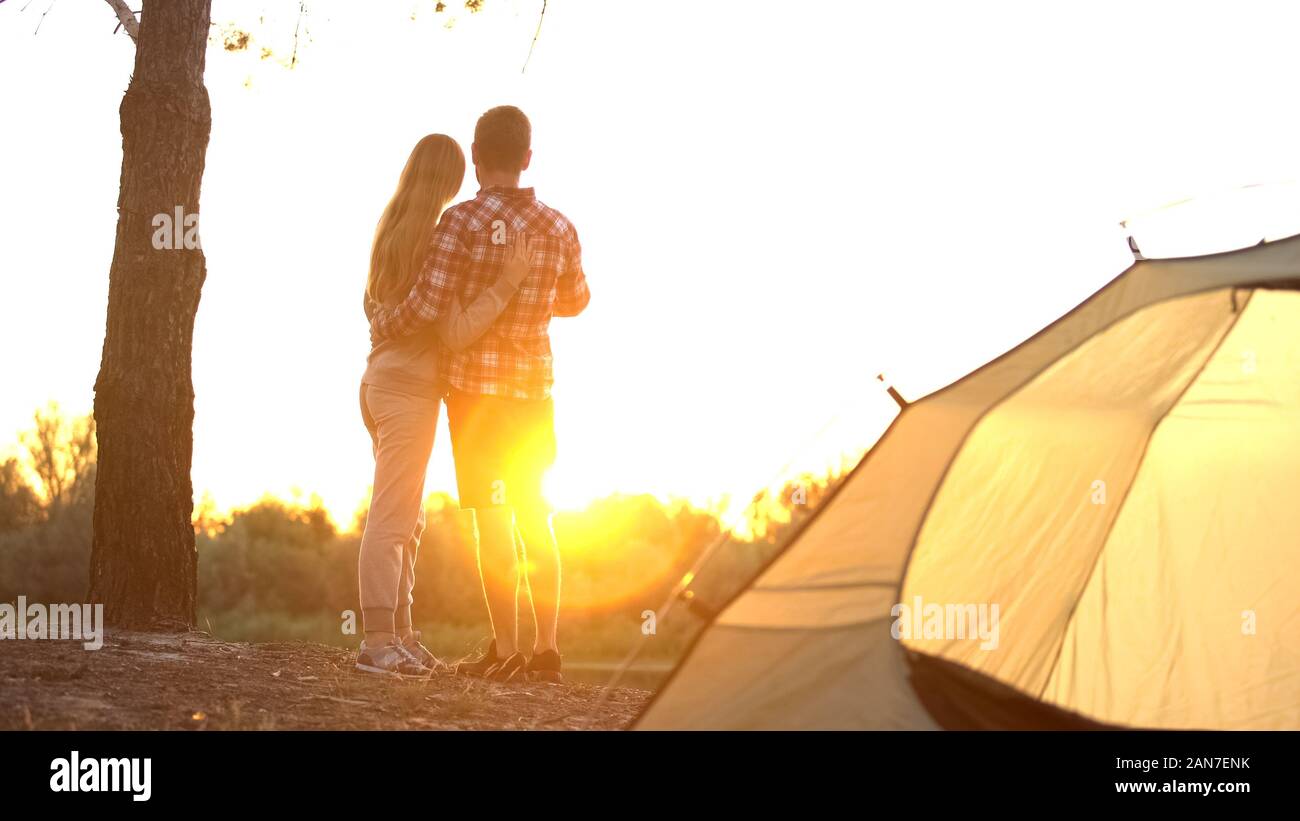 Campers looking at sunset and embracing, enjoying beautiful view, good ...