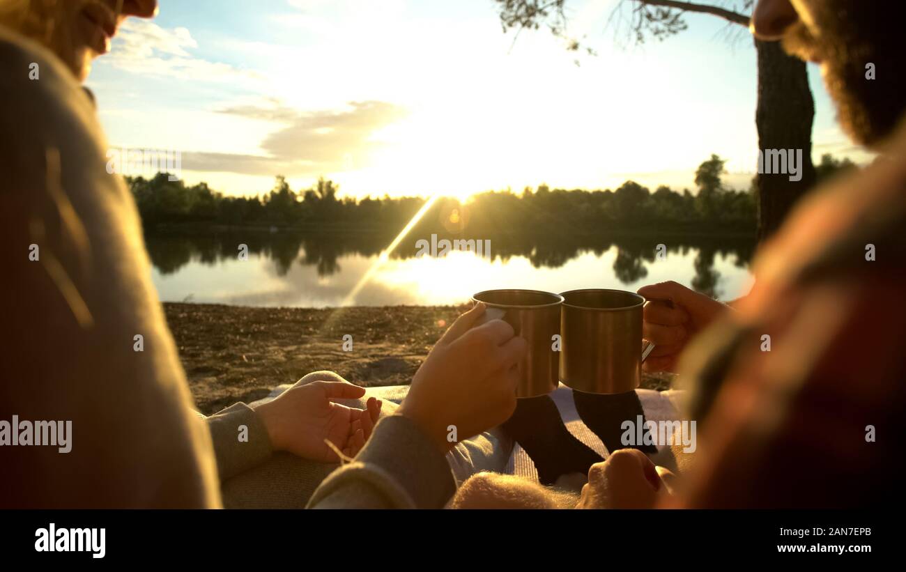 Couple clinking cups together, spending evening in wild, watching ...