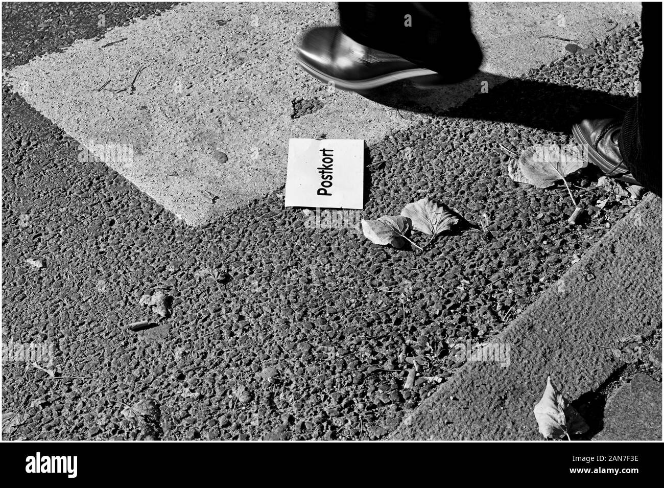 Man's boot stepping over a discarded postcard while crossing the street ...