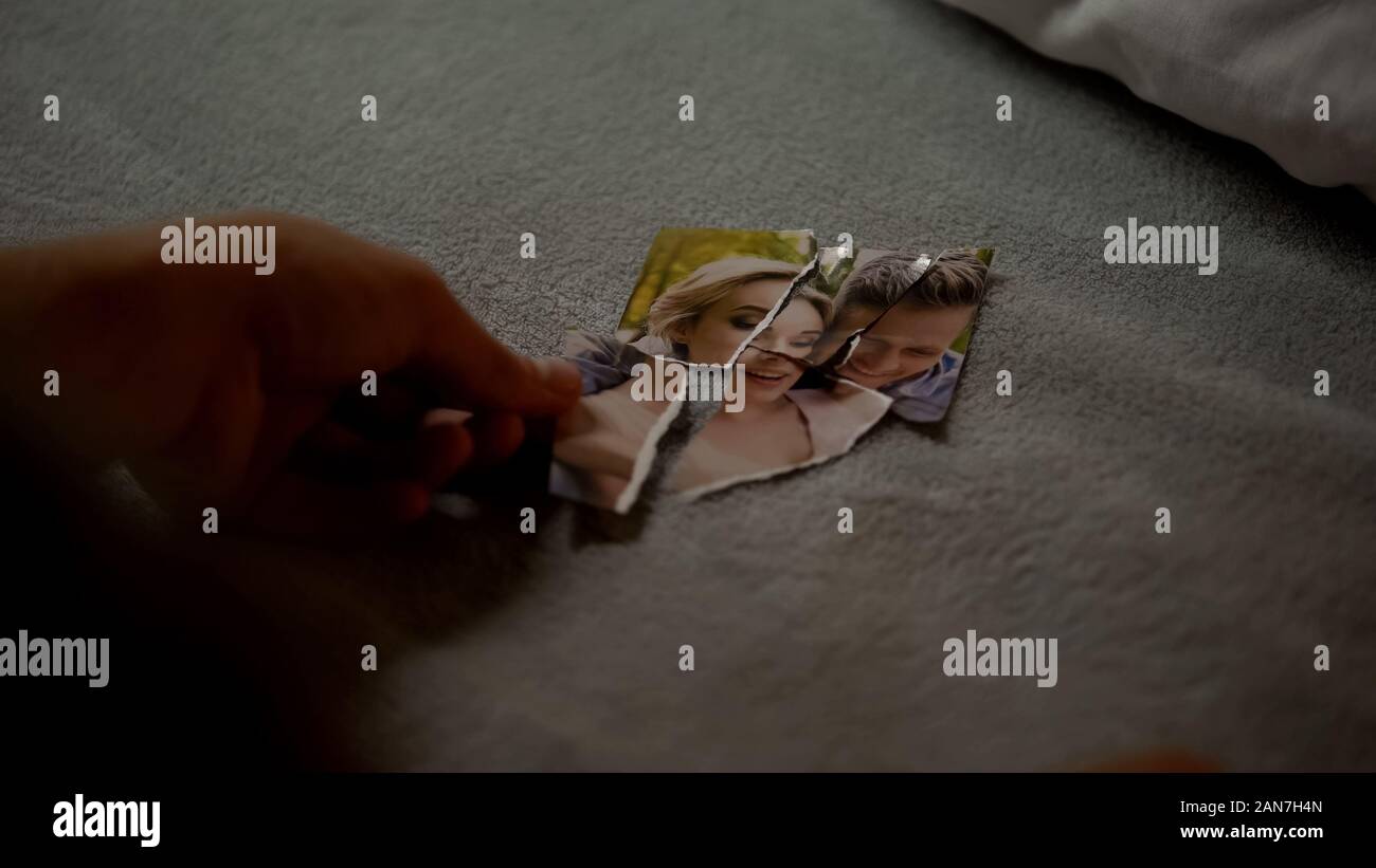 Hands of young male trying to put together parts of torn photo with ...