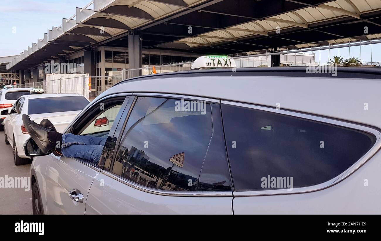 Taxi driver resting car airport parking, legs outside, passenger ...