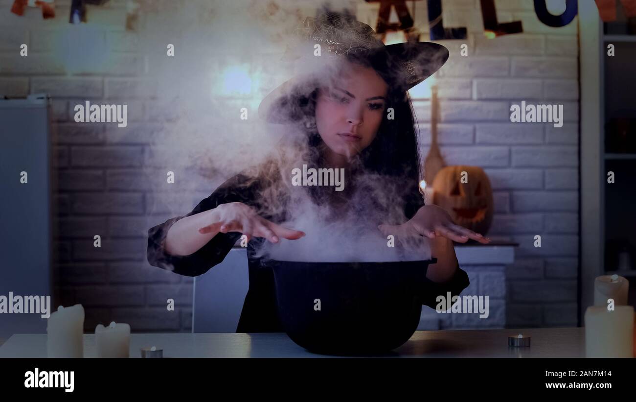 Woman in witch costume making conjuring gestures above magical pot with ...