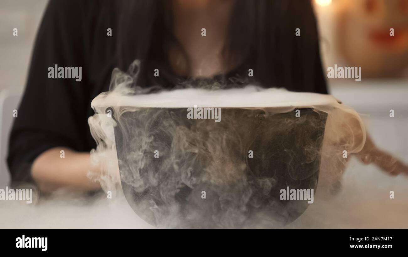 Witch conjuring, putting magic spell and cooking potion in pot with ...