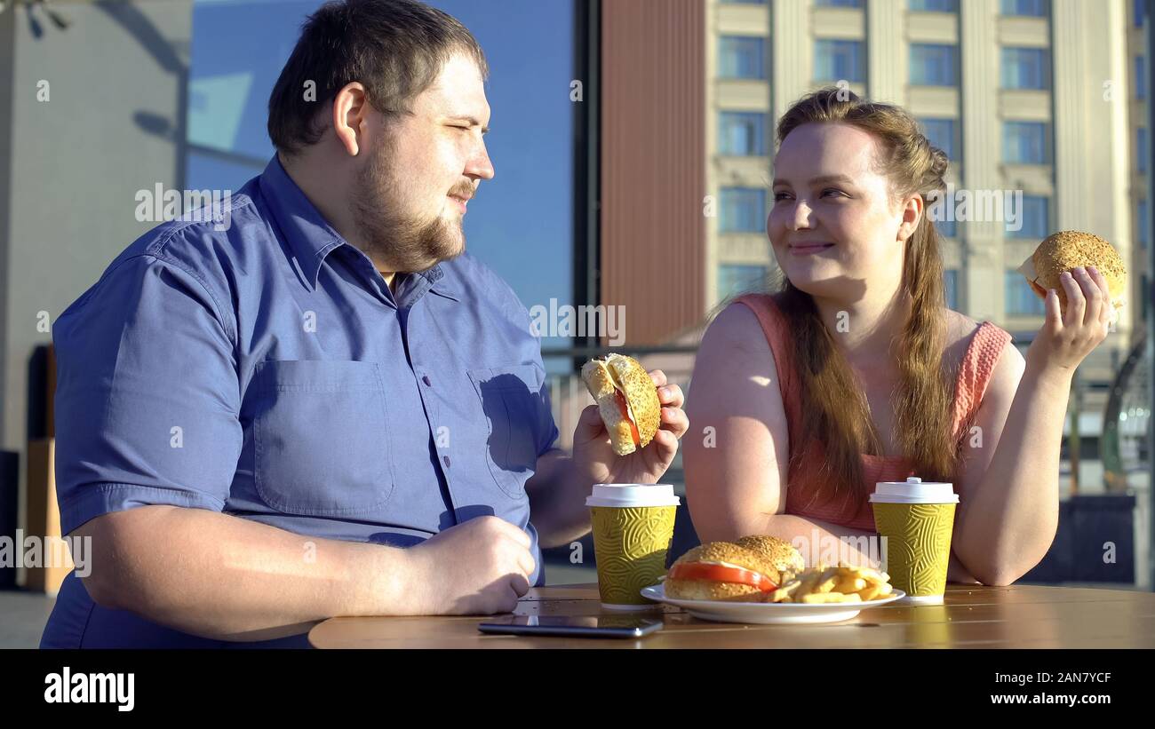 Happy obese couple eating hamburgers on romantic date, flirting in ...