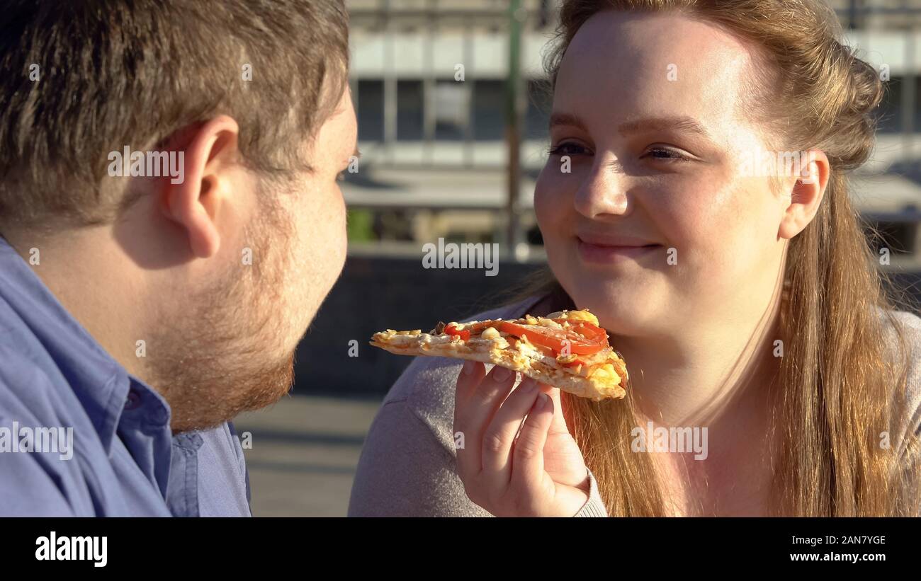 Fat boyfriend and girlfriend eating pizza outdoors romantic date, junk ...