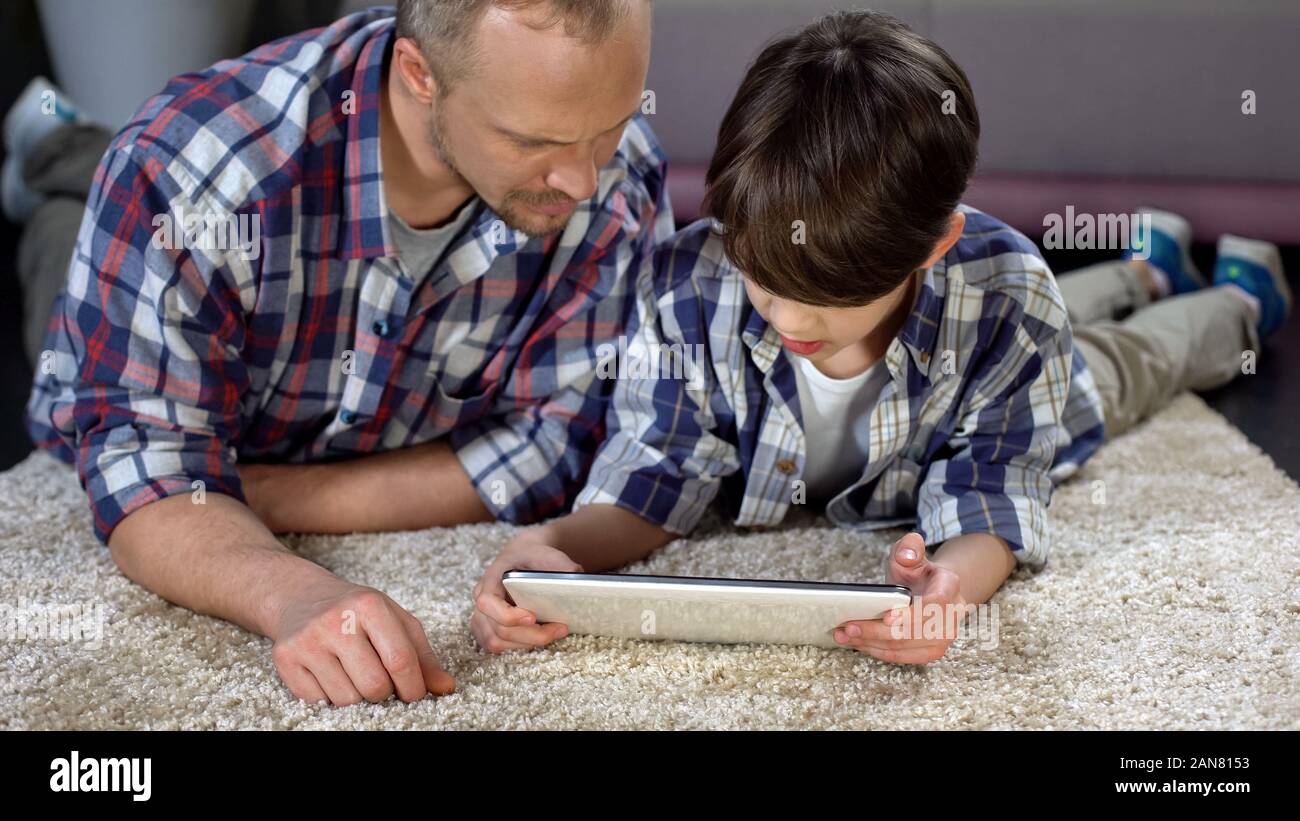 Boy using interactive application on tablet with help of father, family ...