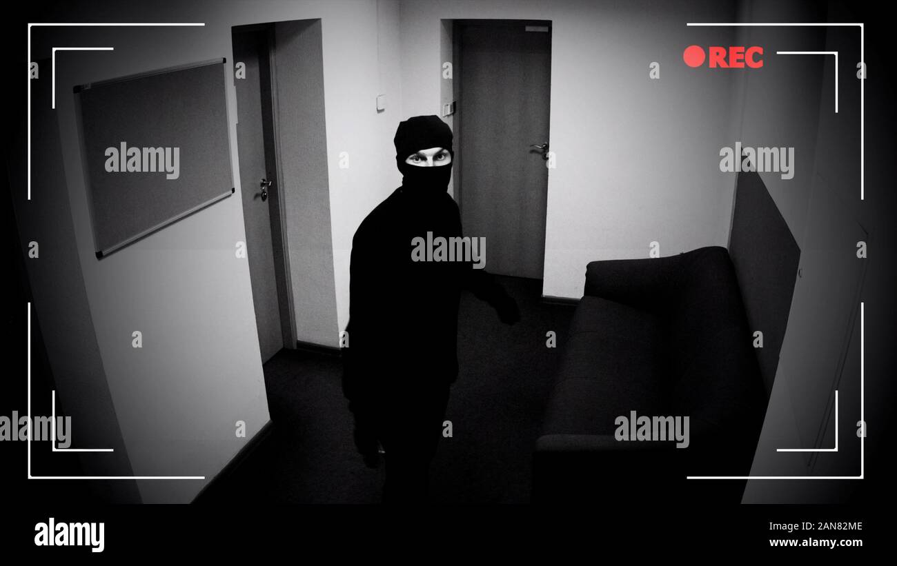 Robber in mask looking surveillance camera, corporative building ...