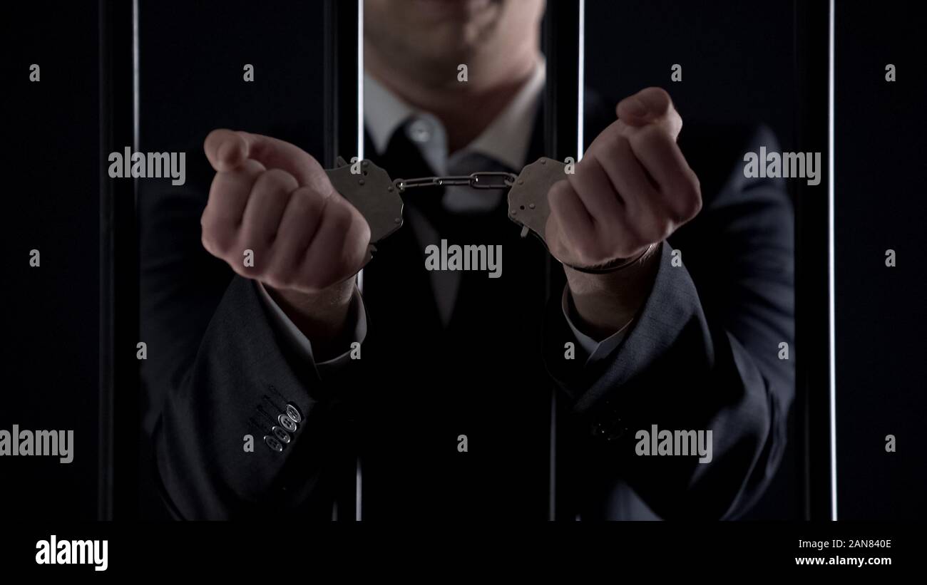Man in suit showing hands in handcuffs behind bars, bribery, financial ...