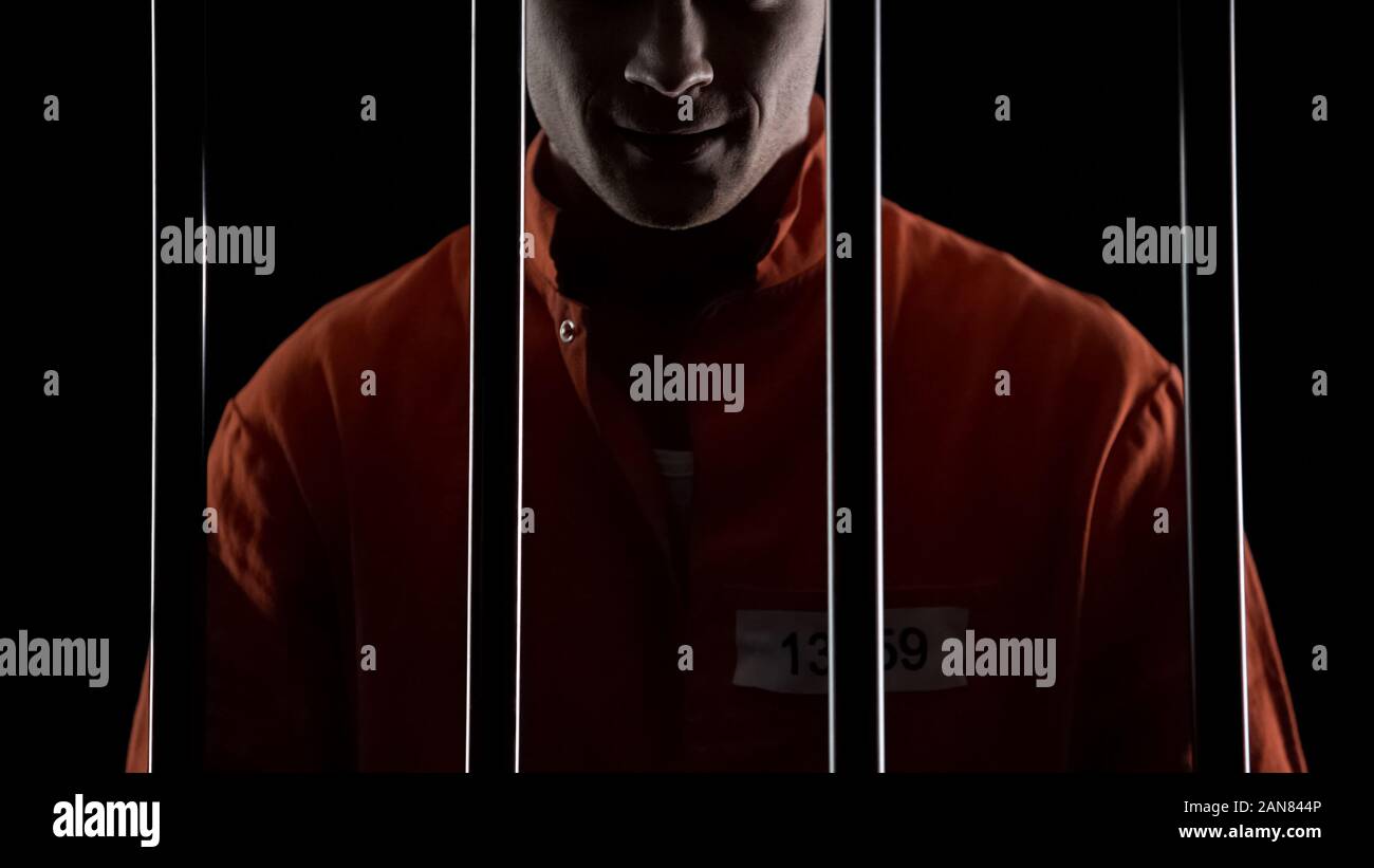 Mad serial killer standing behind prison bars and smirking, mental ...