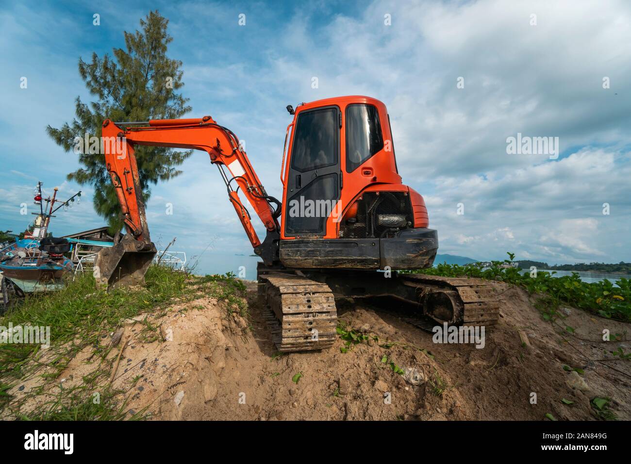 Small orange excavator on a ground against blue sky and sea for a works ...
