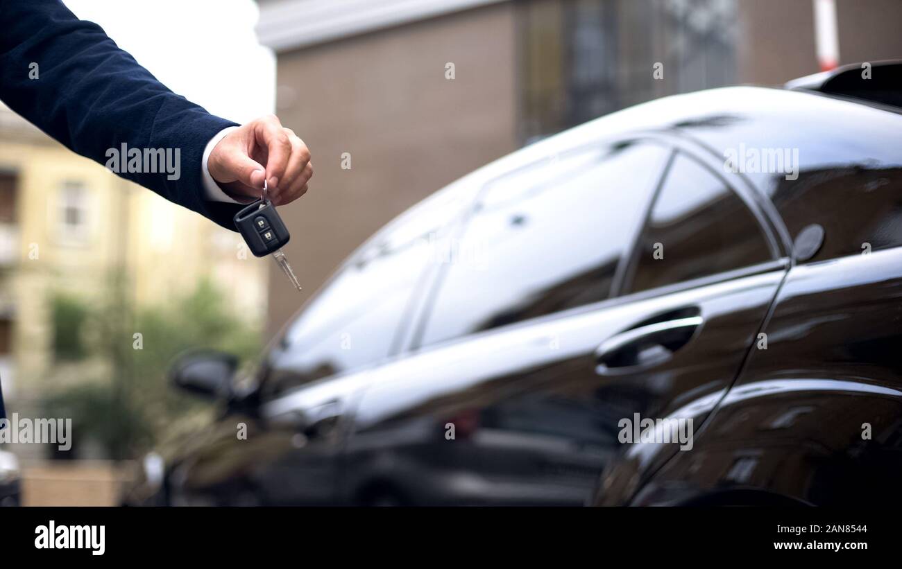 Salesman giving car key to buyer, dealership showroom, auto rental ...