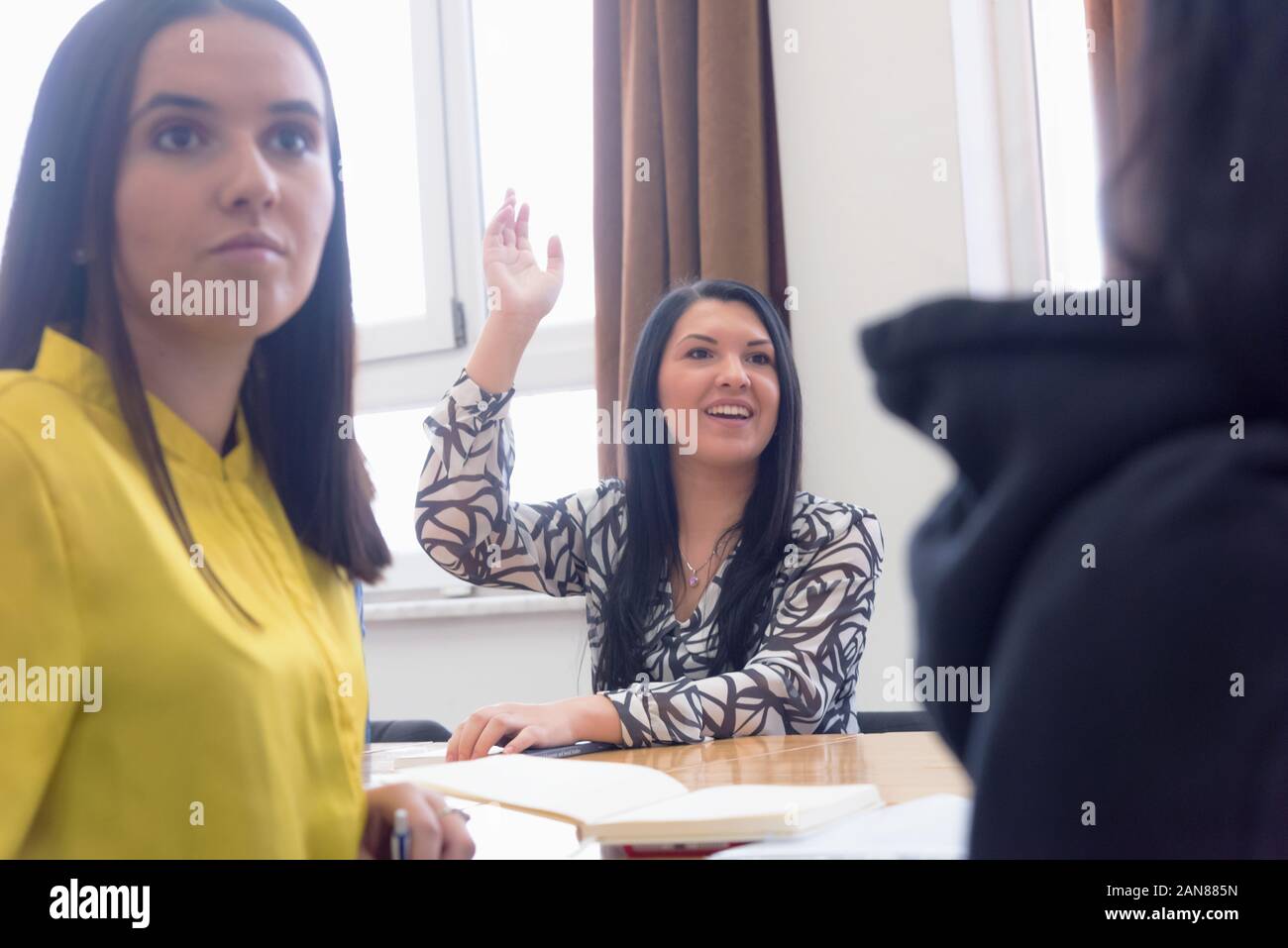 Front view of female student sitting in the class and raising hand up ...