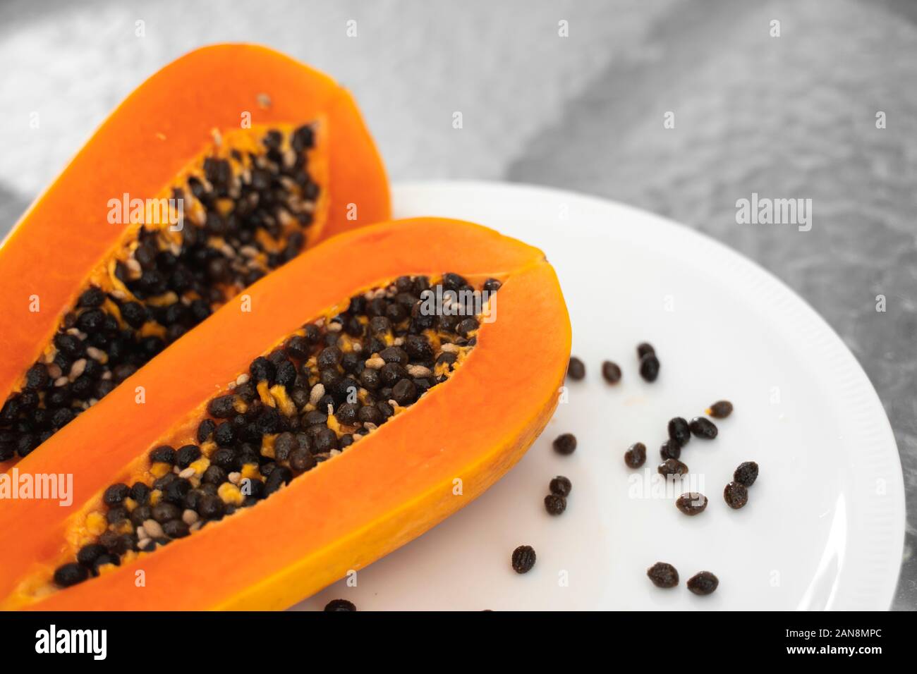 Half cut ripe papaya with seed on a white plate. Slices of sweet papaya ...