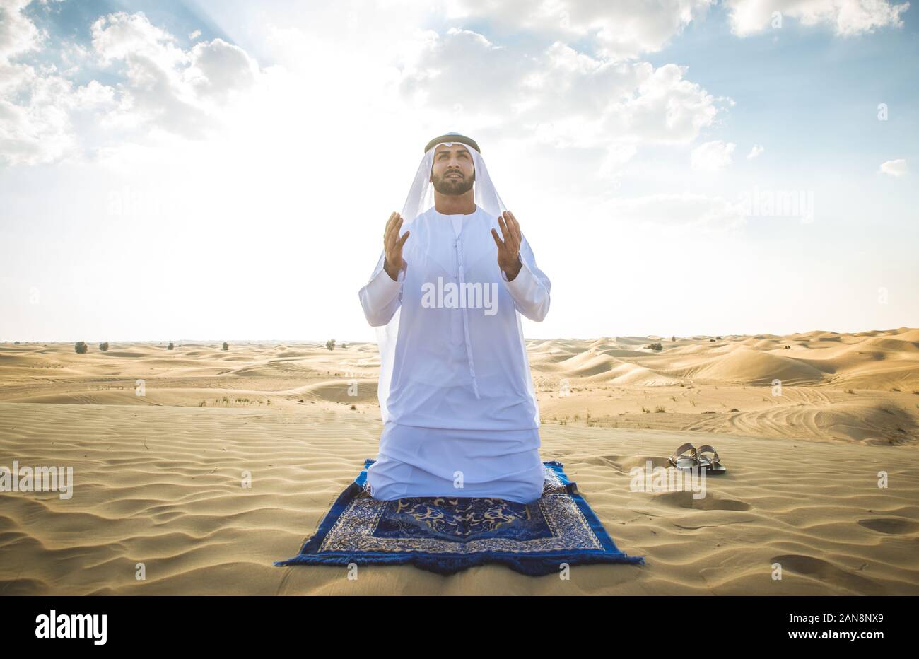 Man with white traditional kandura from uae praying in the desert on ...