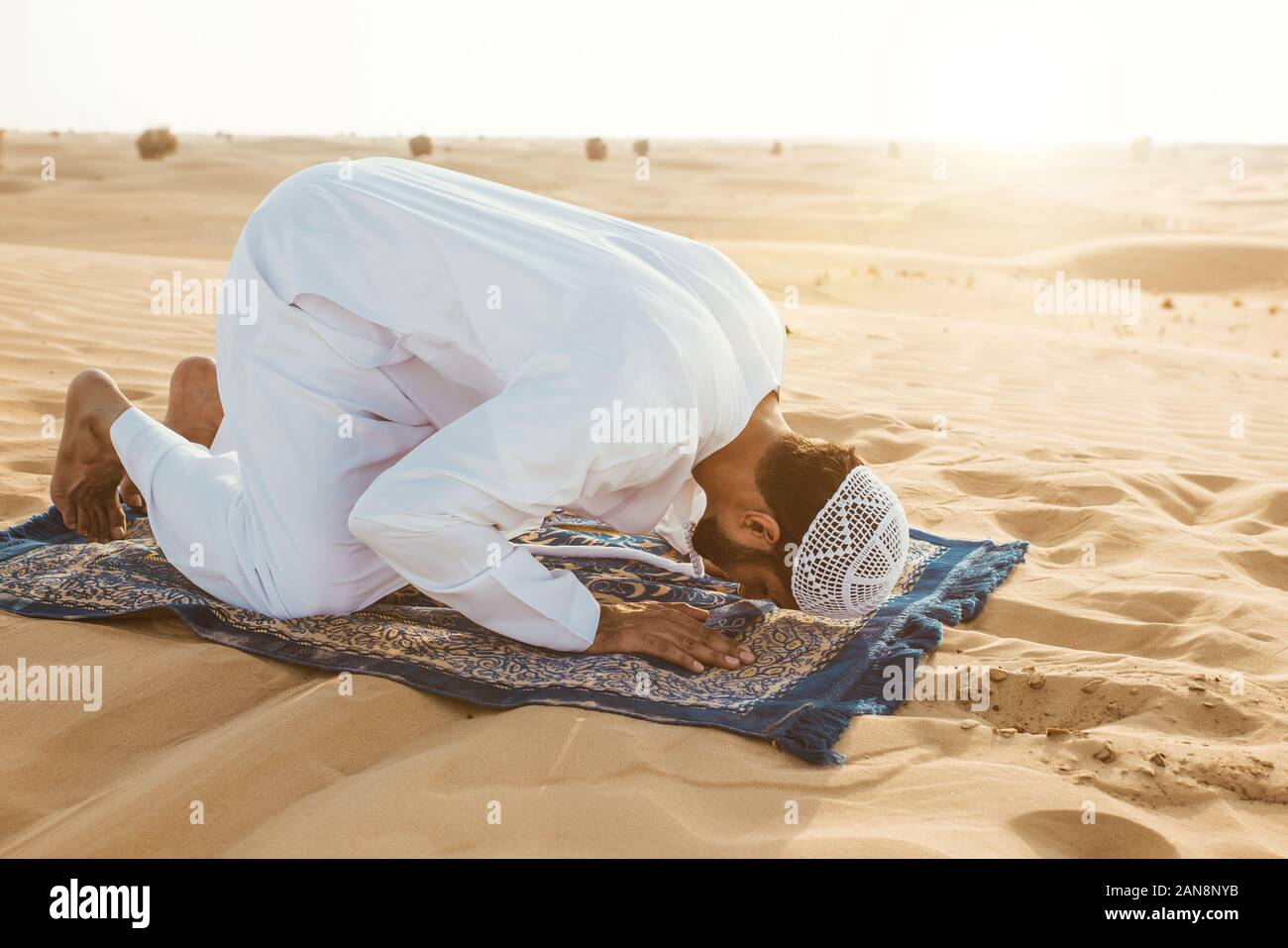Man with white traditional kandura from uae praying in the desert on ...