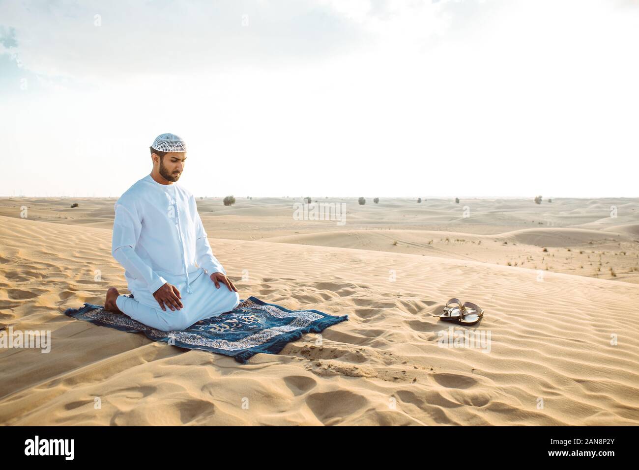 Man with white traditional kandura from uae praying in the desert on ...