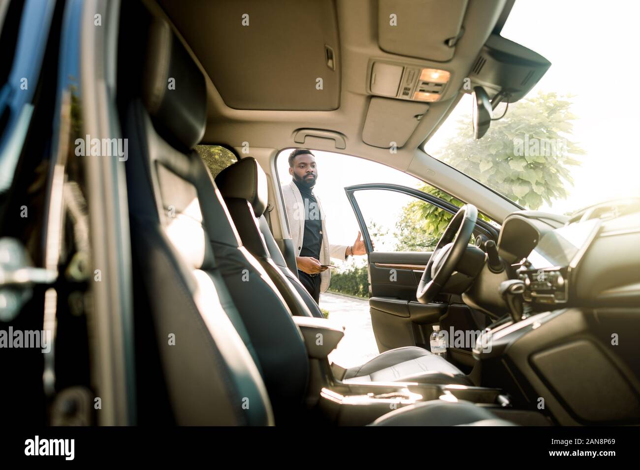 Busy African young man in suit getting in car. Happy young businessman ...