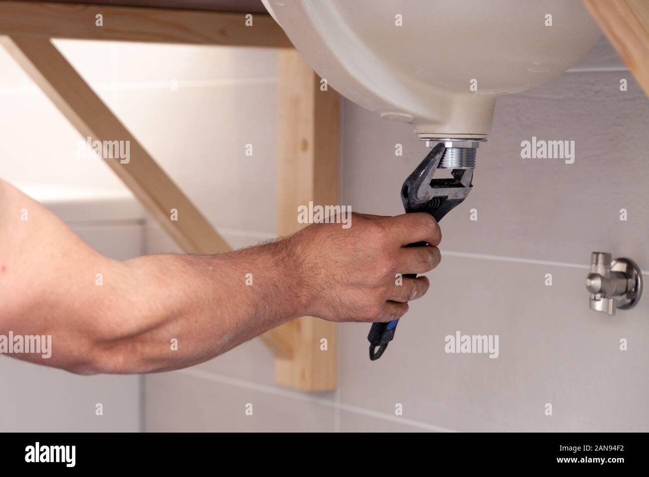 Closeup male plumber's hand fixing sink in bathroom with tile wall ...