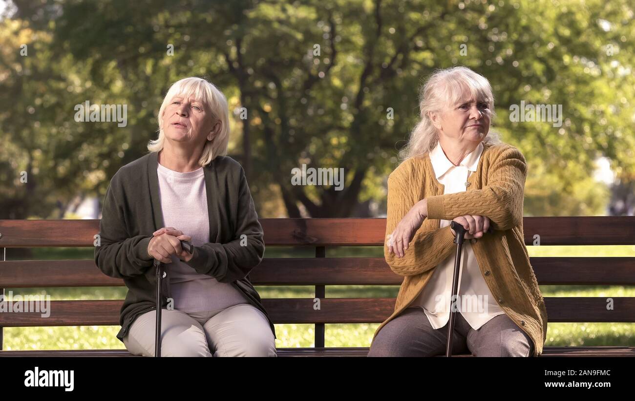 Mature ladies sitting separately on bench in park, friends argued and ...