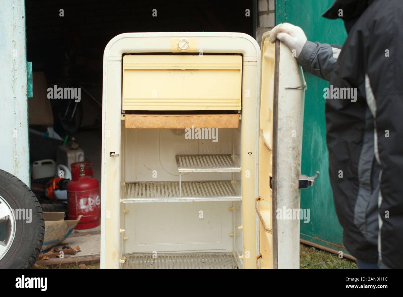 A man about to discard old fridge standing next to the open garage door ...