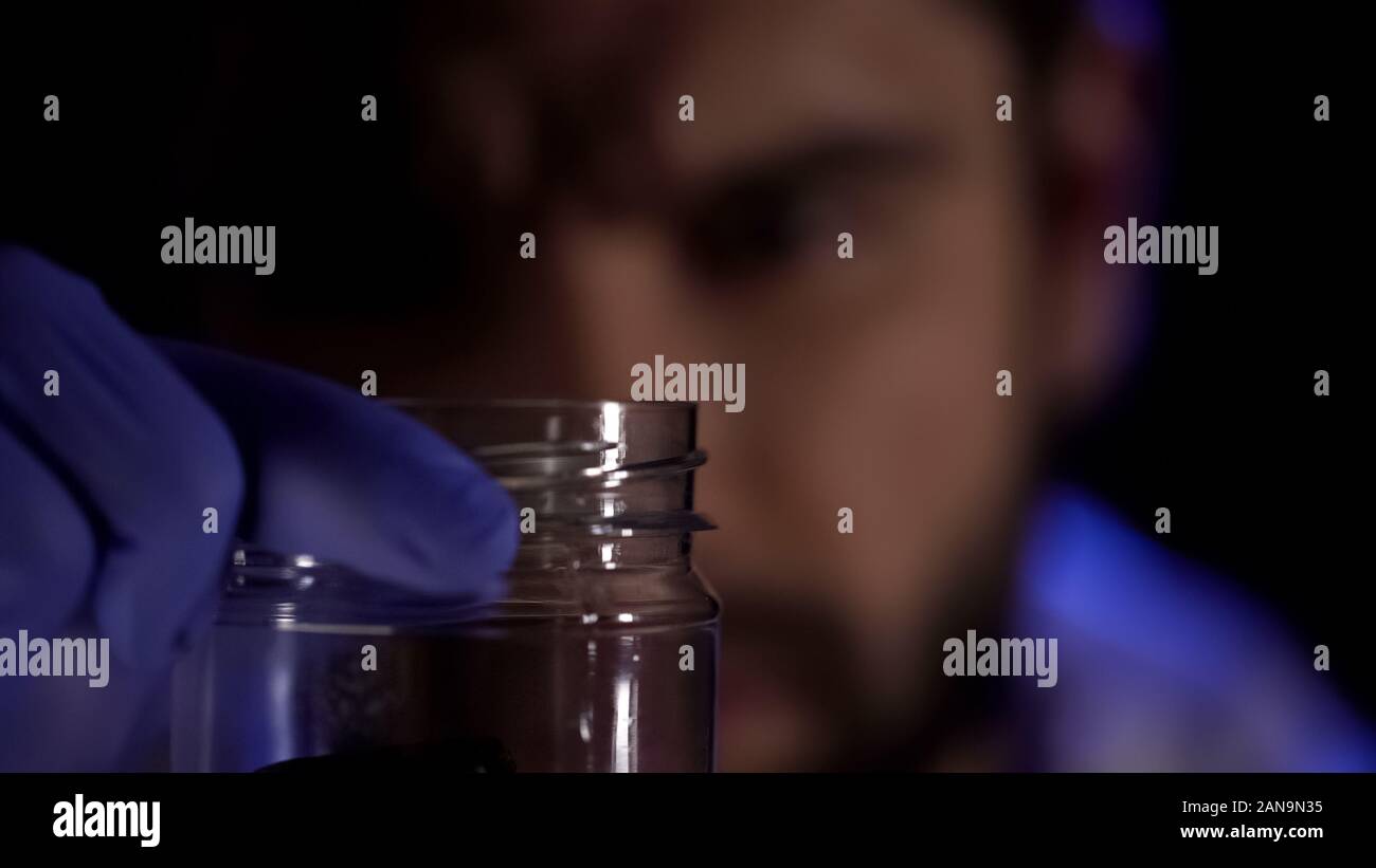 Forensic scientist holding glass jar in hands, examining crime scene ...