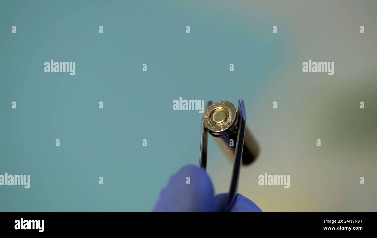 Gun bullet in tweezers examined by criminalist closeup, ballistics ...