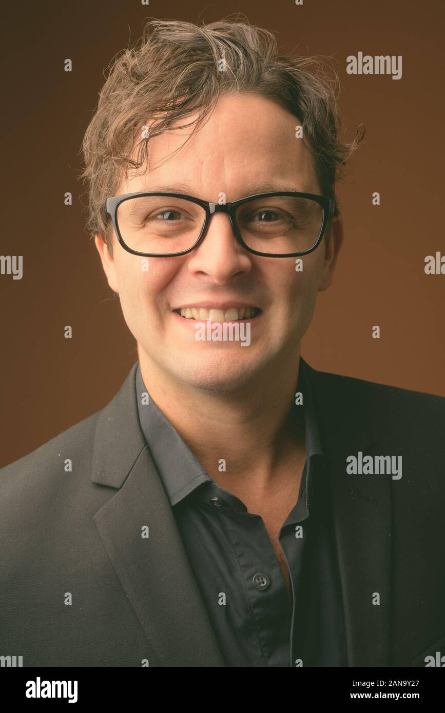 Studio shot of Italian businessman wearing black suit against brown ...