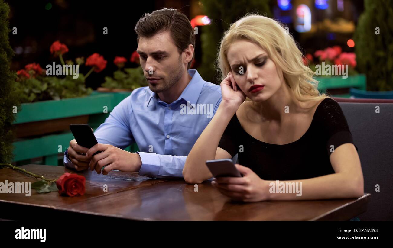 Two young people boring on date, using smartphones, problems in ...