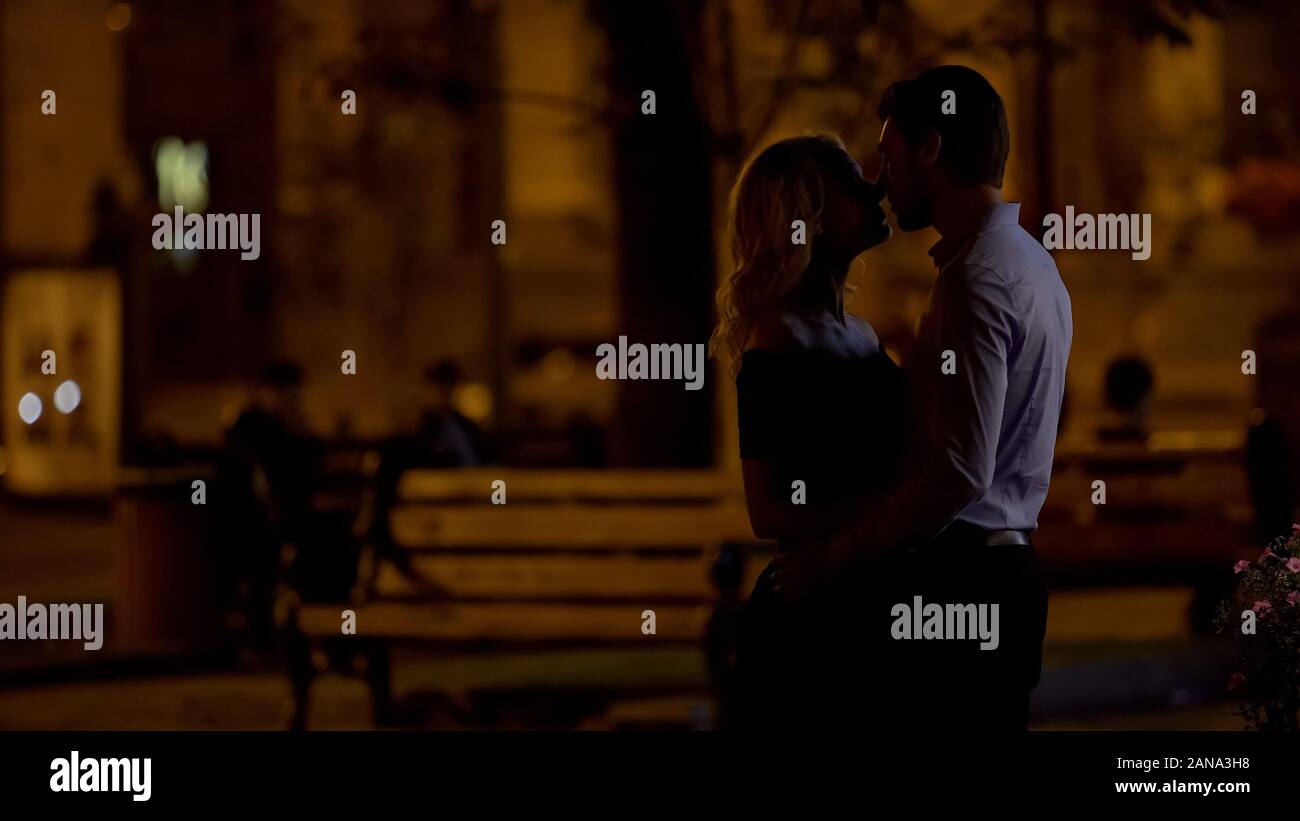 Silhouettes of couple kissing in city park, feeling love emotions at ...