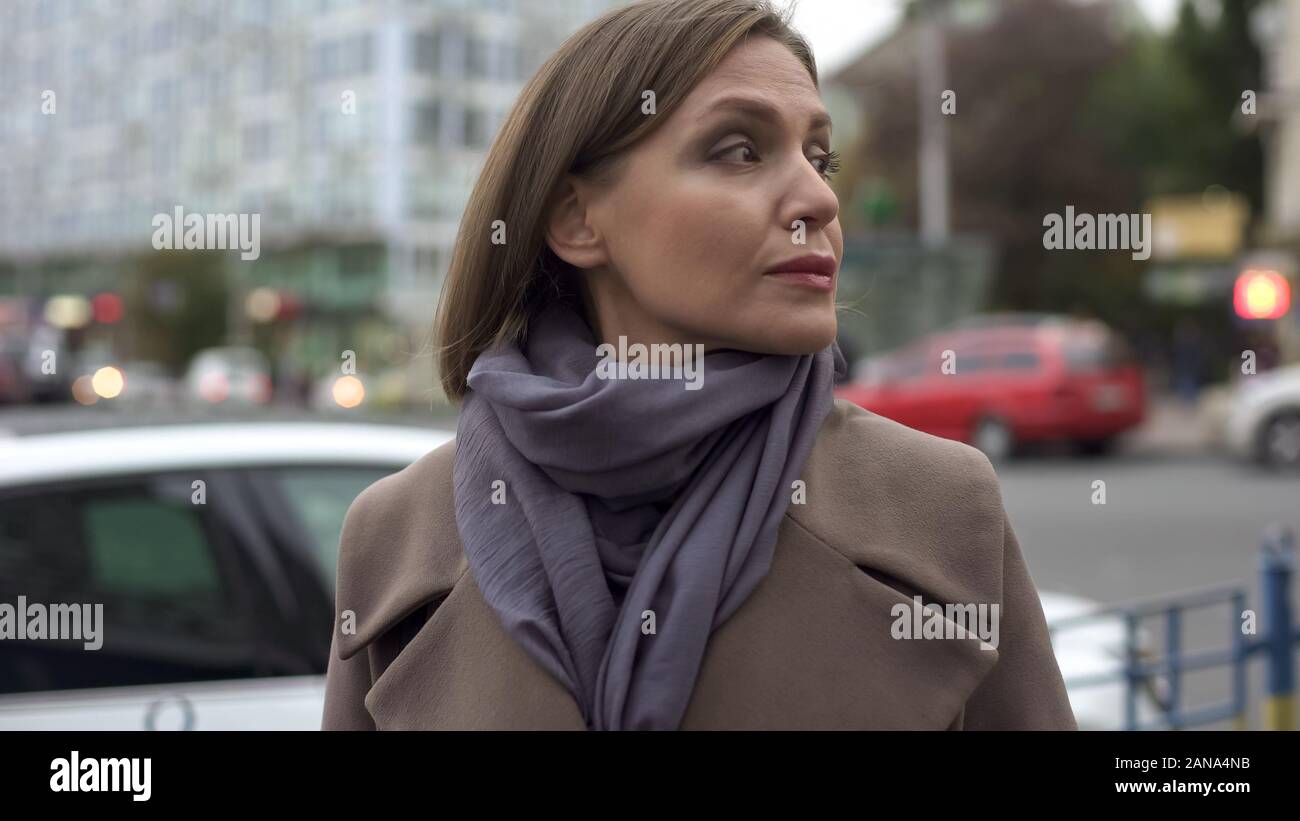 Worried woman standing on busy street, looking around waiting for ...