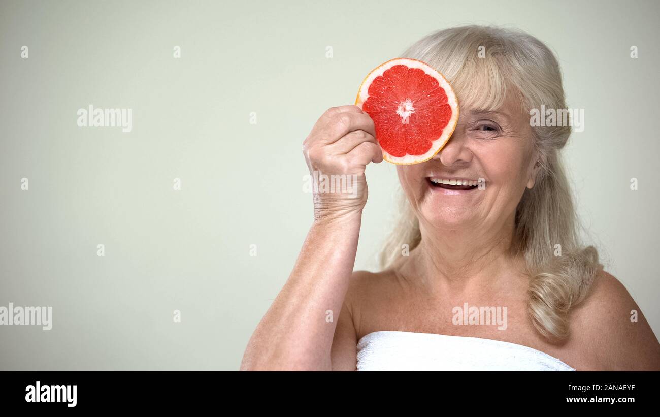 Cheerful smiling elderly lady closing eye with grapefruit slice ...