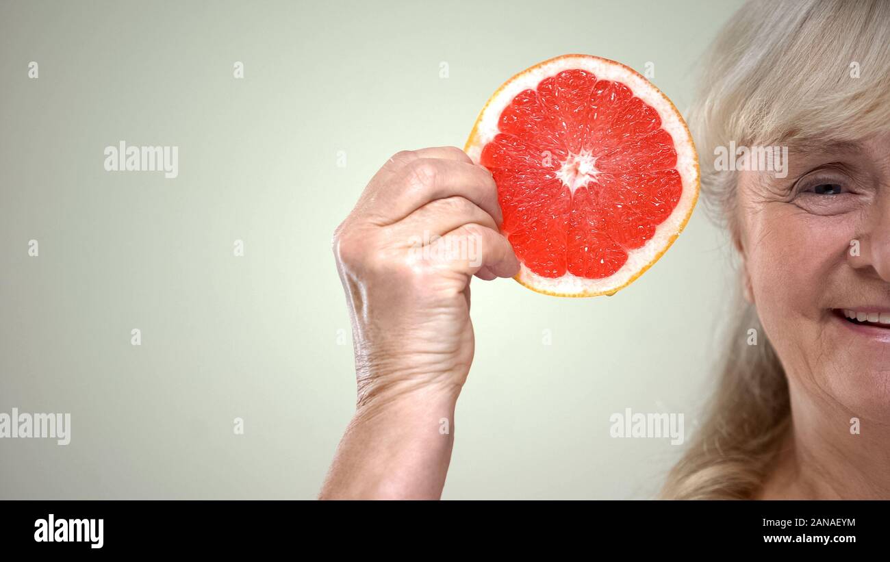 Happy smiling aged woman showing slice of juicy grapefruit, half-face ...