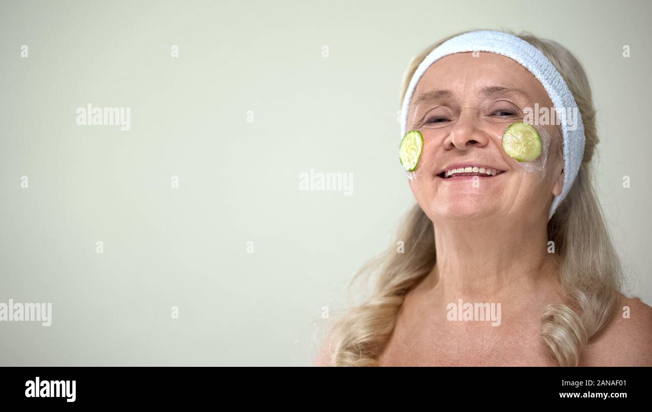 Positive old lady applying cucumber face mask, optimistic attitude to ...
