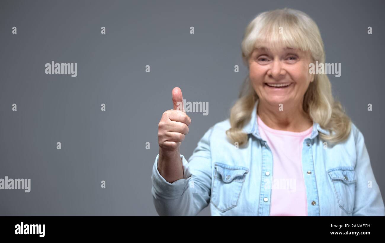 Satisfied elderly woman showing thumbs-up gesture, happy medical clinic ...