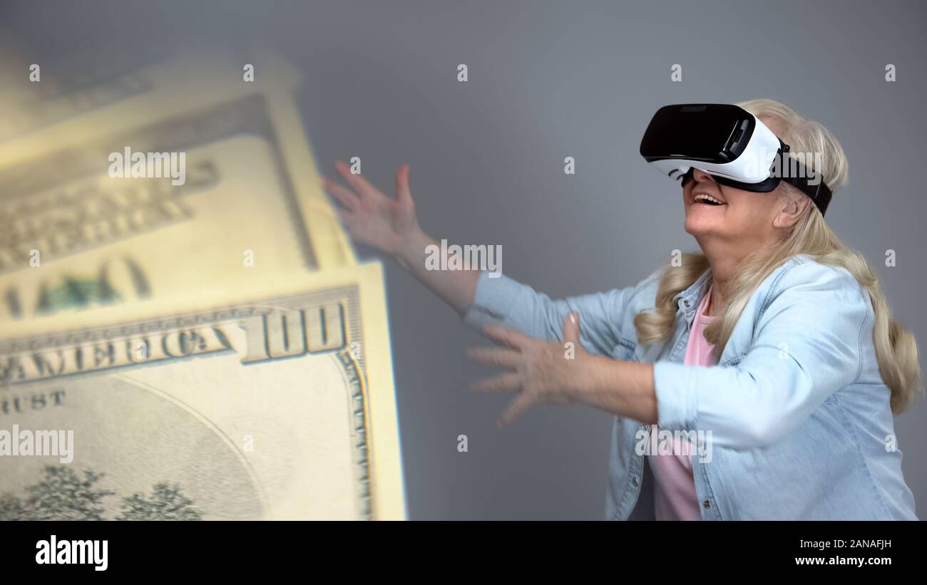 Elderly lady in VR headset trying to catch dollar banknotes, banking ...