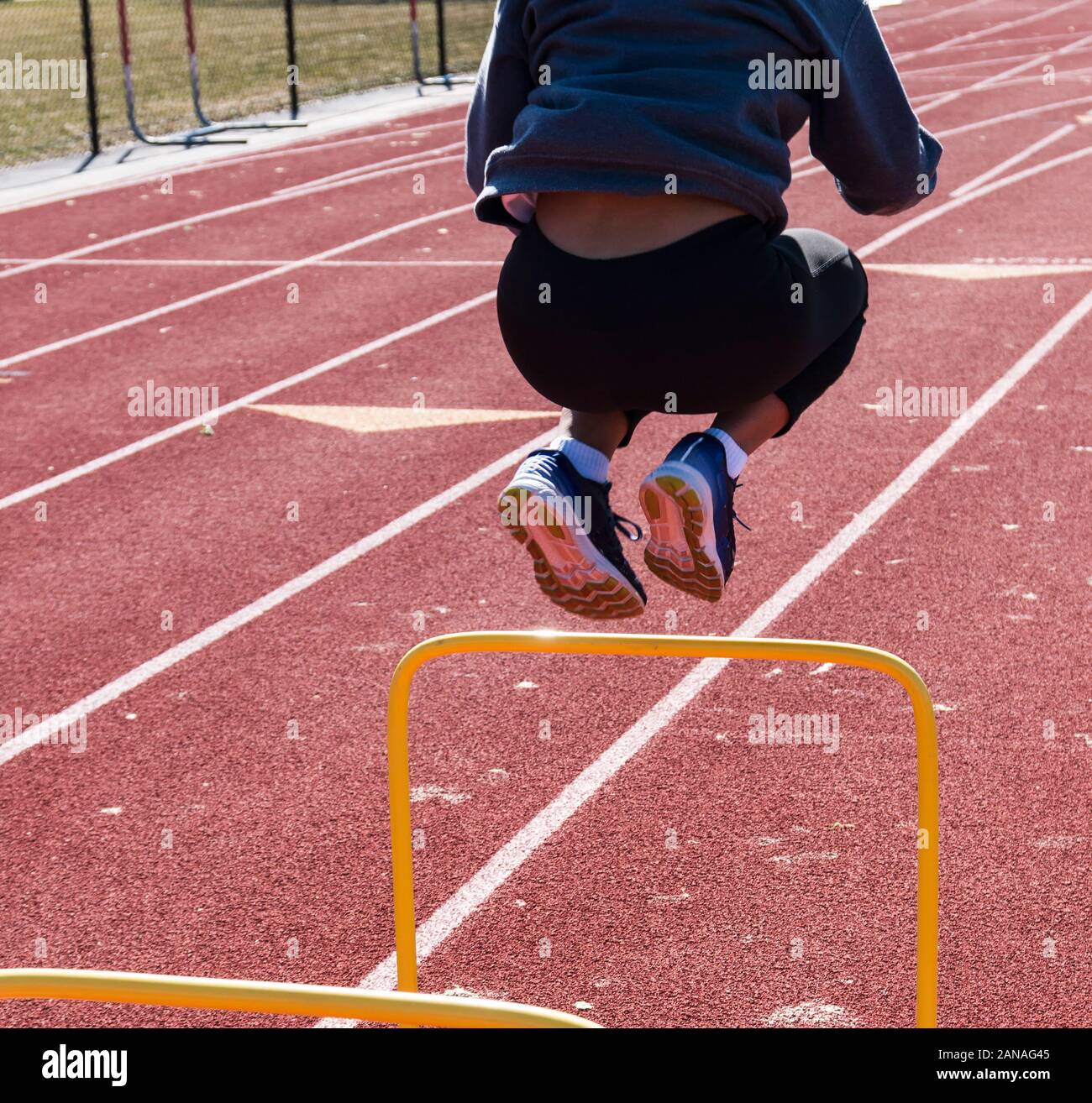 A high school athlete is jumping over a 2 foot high yellow hurdle on a ...