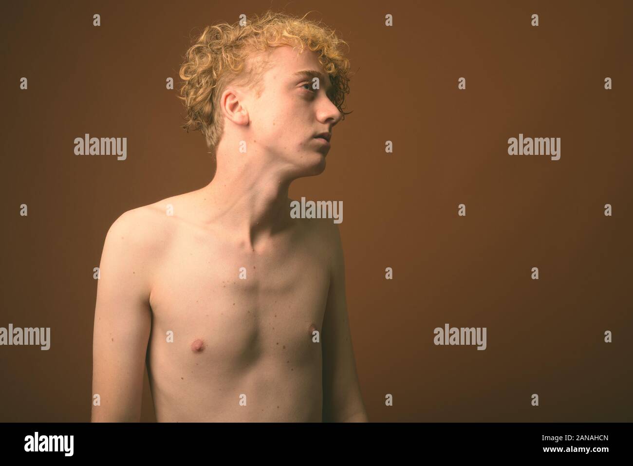 Studio Shot Of Skinny Young Man With Curly Hair Shirtless Against Brown