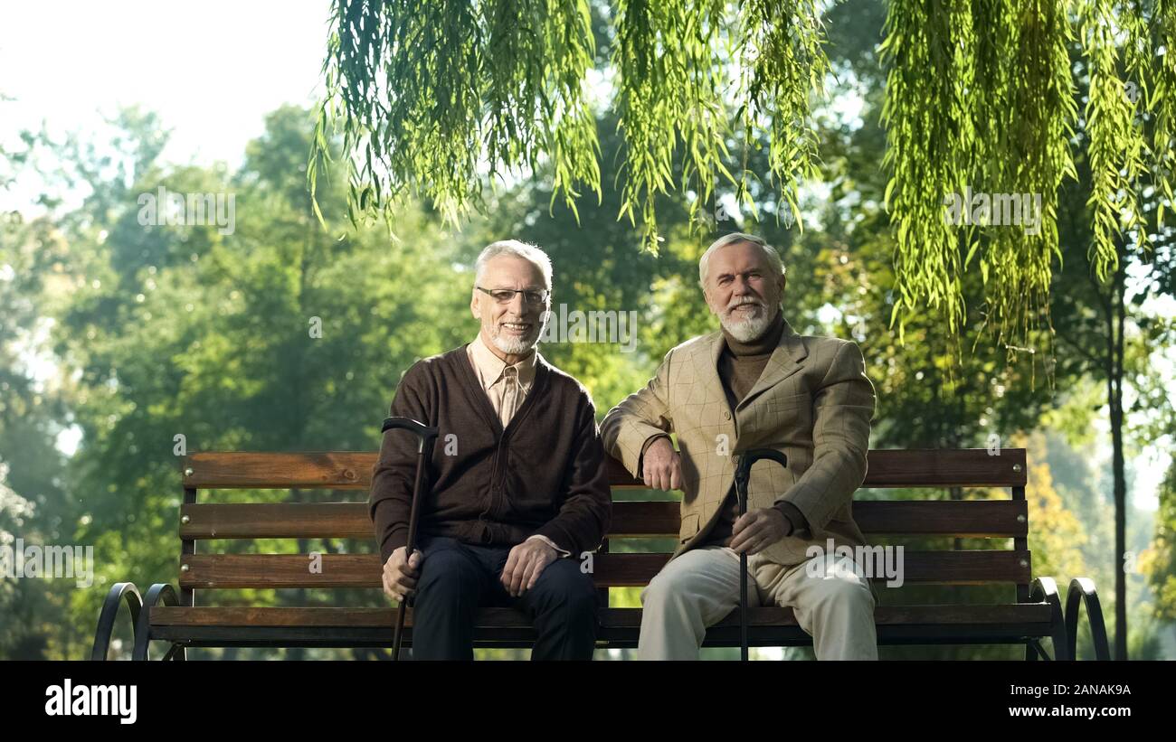 Cheerful senior men with walking sticks sitting on bench, happy life in ...