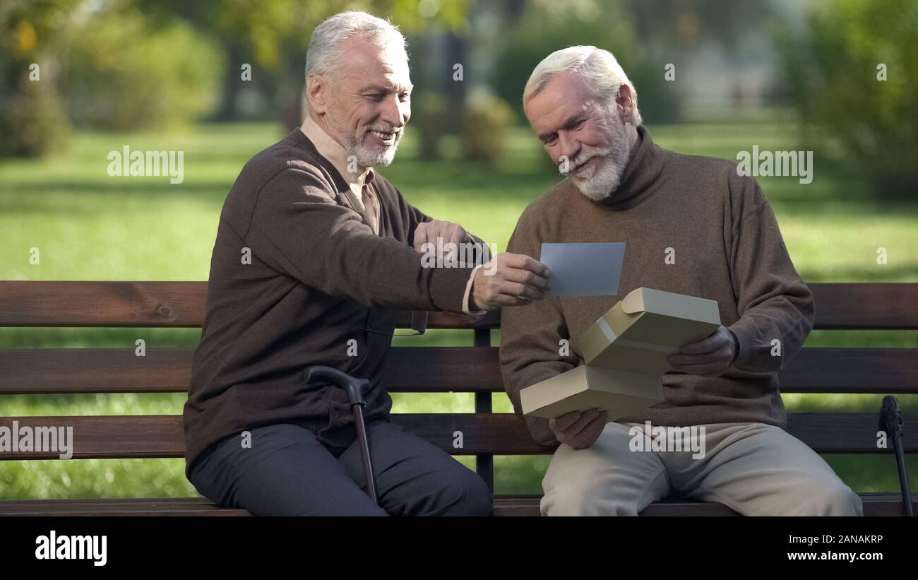 Two male friends on park bench looking at photo and smiling, old time ...