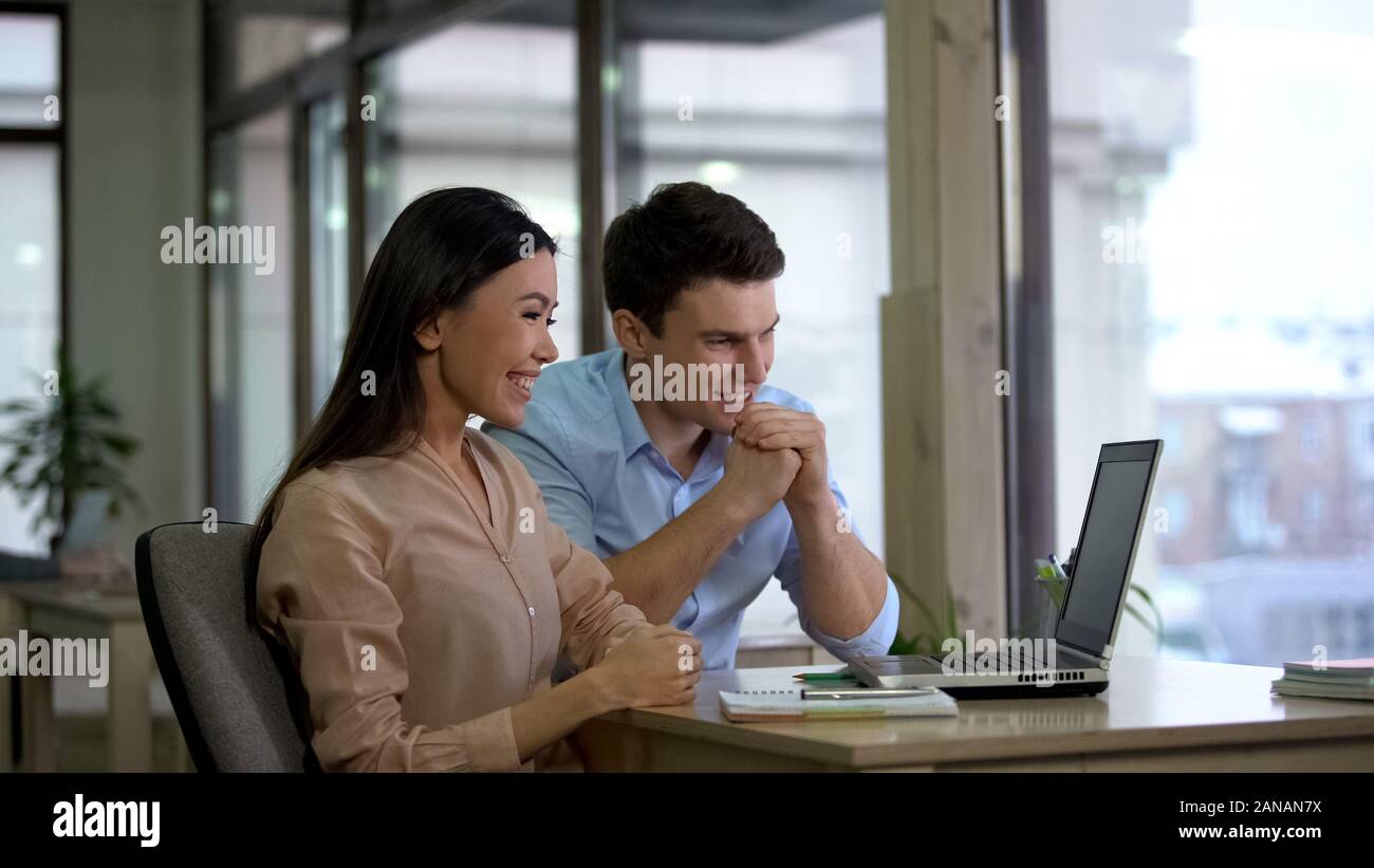 Young smiling colleagues looking laptop together sitting office table ...