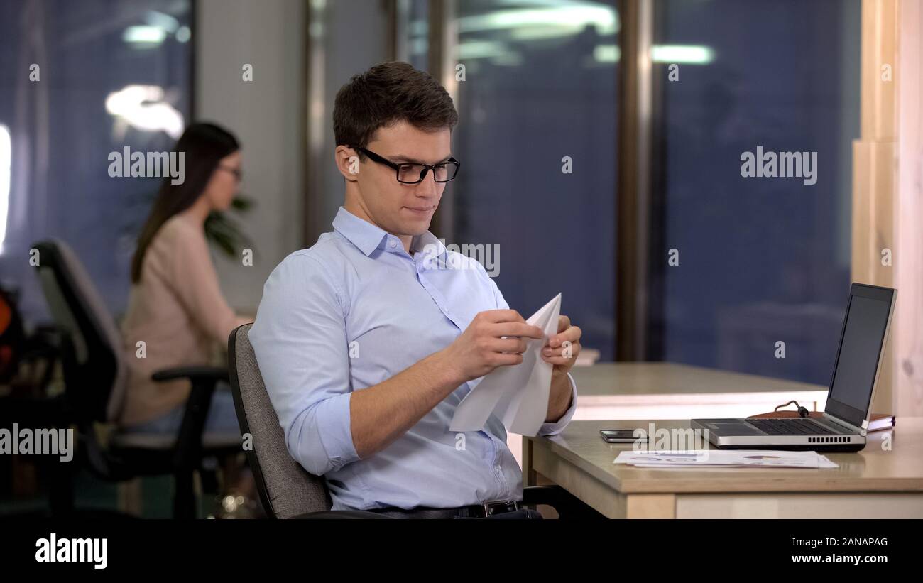 Playful male making paper plane in office, tired monotonous routine ...