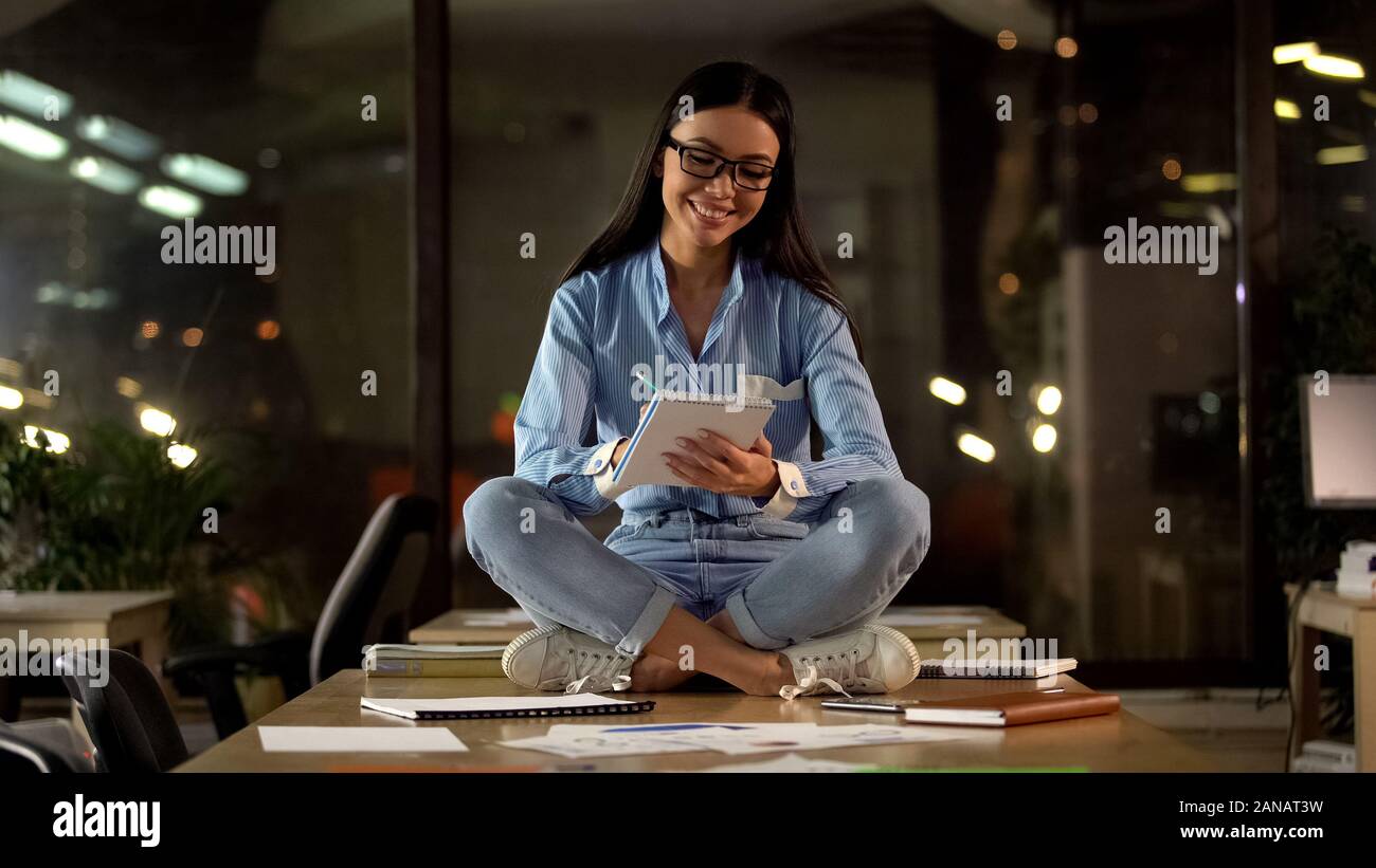 Positive female sitting lotus pose writing in notebook, modern work ...