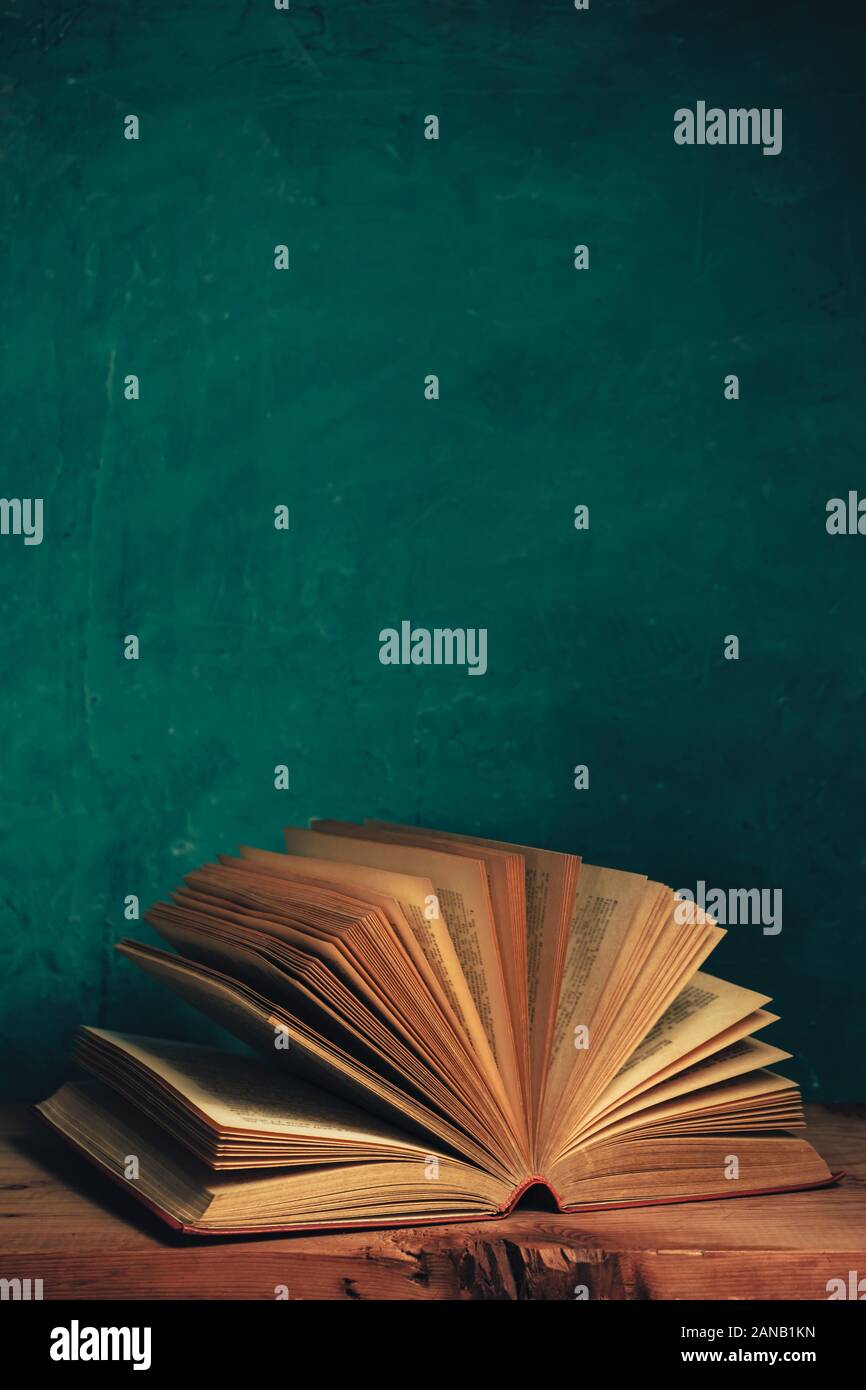 Open old book on a old oak wooden table and green wall background ...
