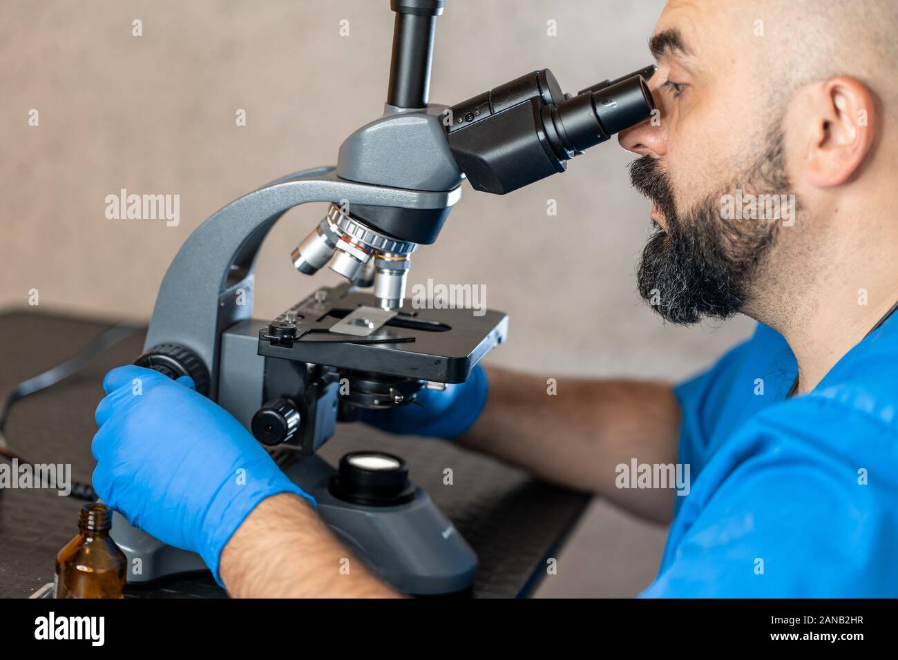 Male laboratory assistant examining biomaterial samples in a microscope ...