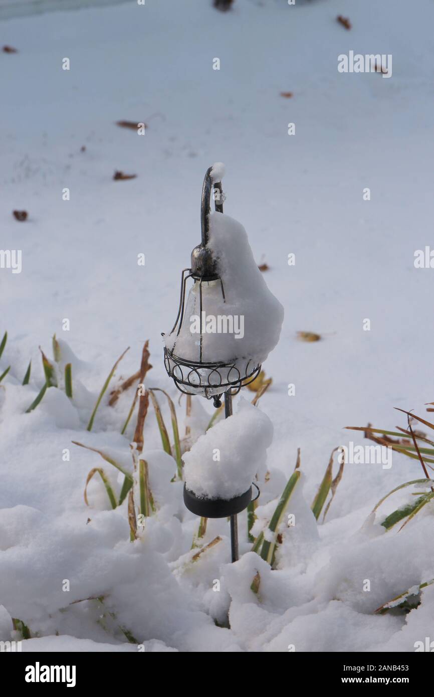 Snow piled high on a solar light and iris leaves after an early ...