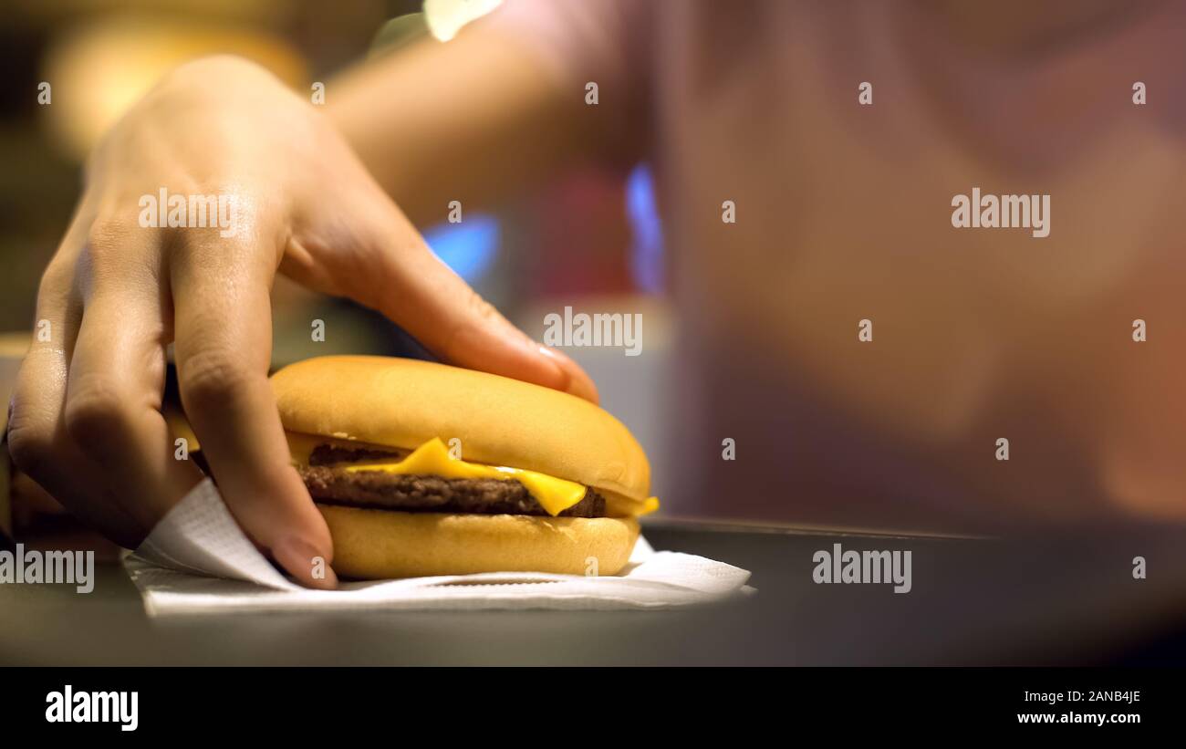 Woman taking cheeseburger from table, dinner in fast food restaurant ...